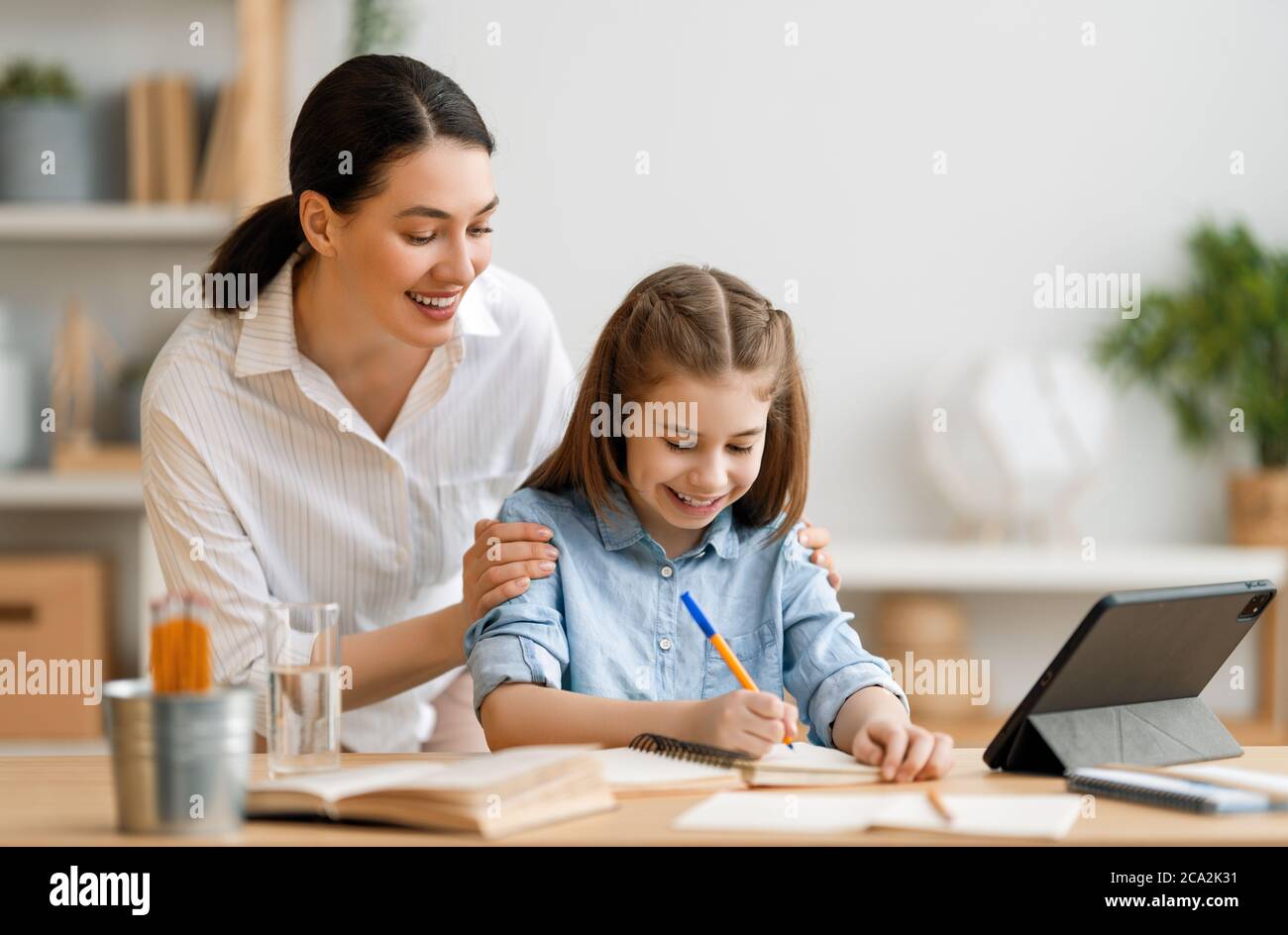 Back to school. Happy child and adult are sitting at desk. Girl doing ...