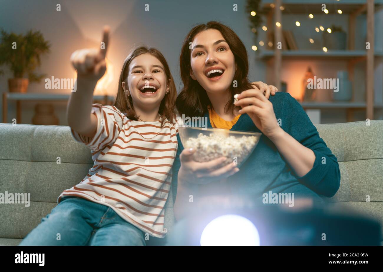 Happy family watching projector, TV, movies with popcorn in the evening ...