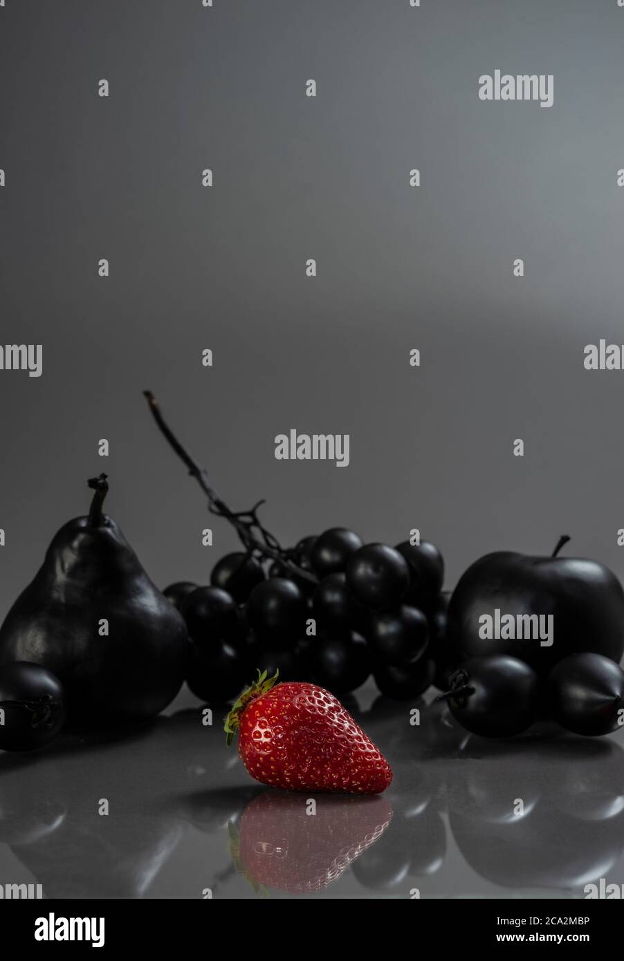 Conceptual image of black fruits on gray reflective surface with a red ...