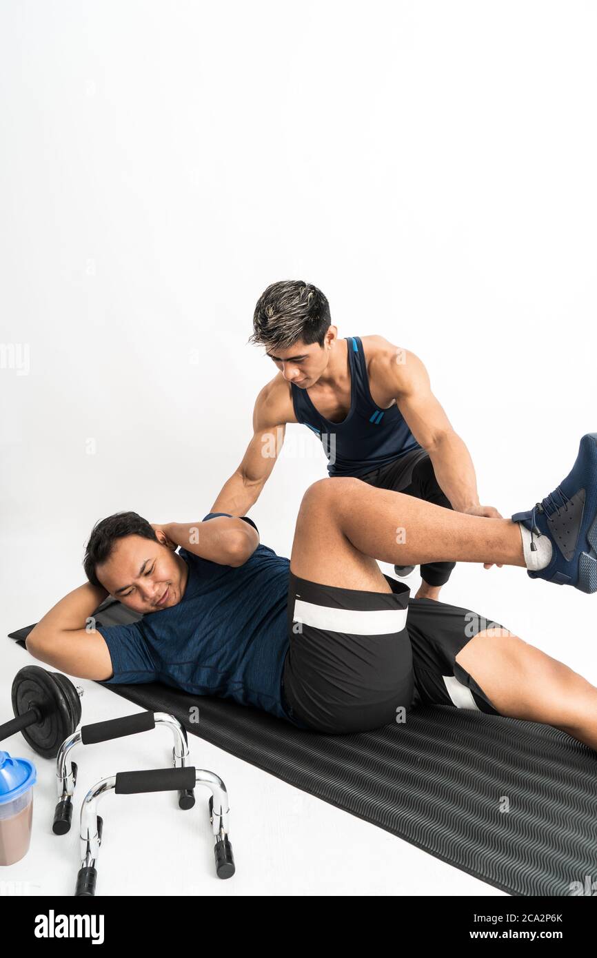 trainer accompanies a man doing sit up exercises holding back to make ...