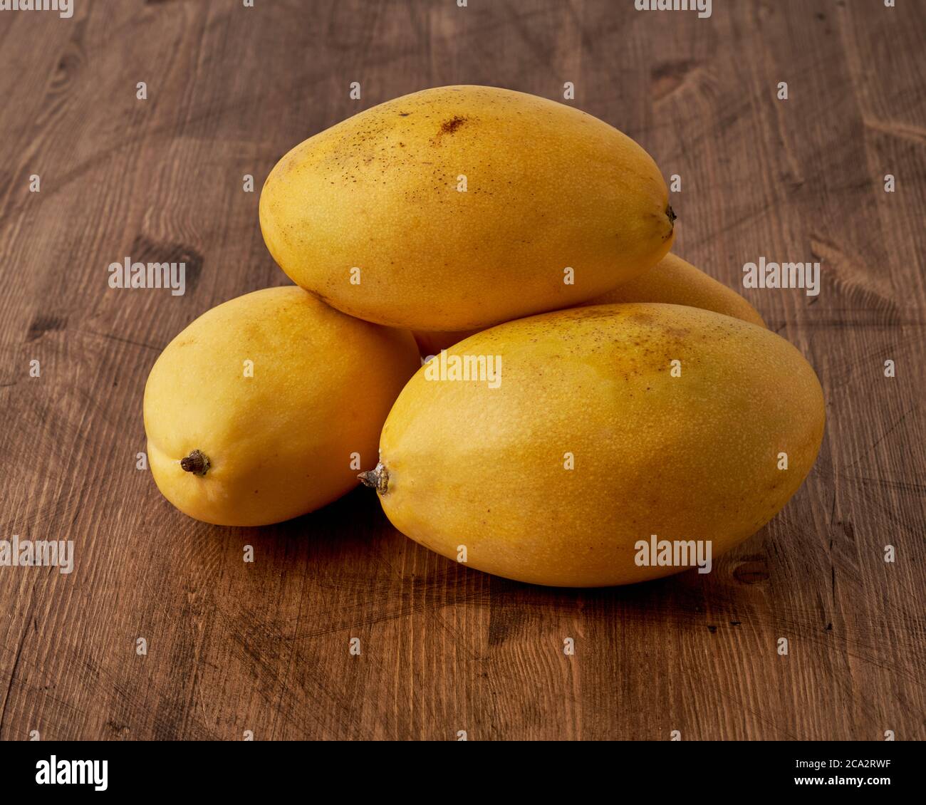 Four whole fruit mangoes on wooden table. Large juicy bright ripe ...