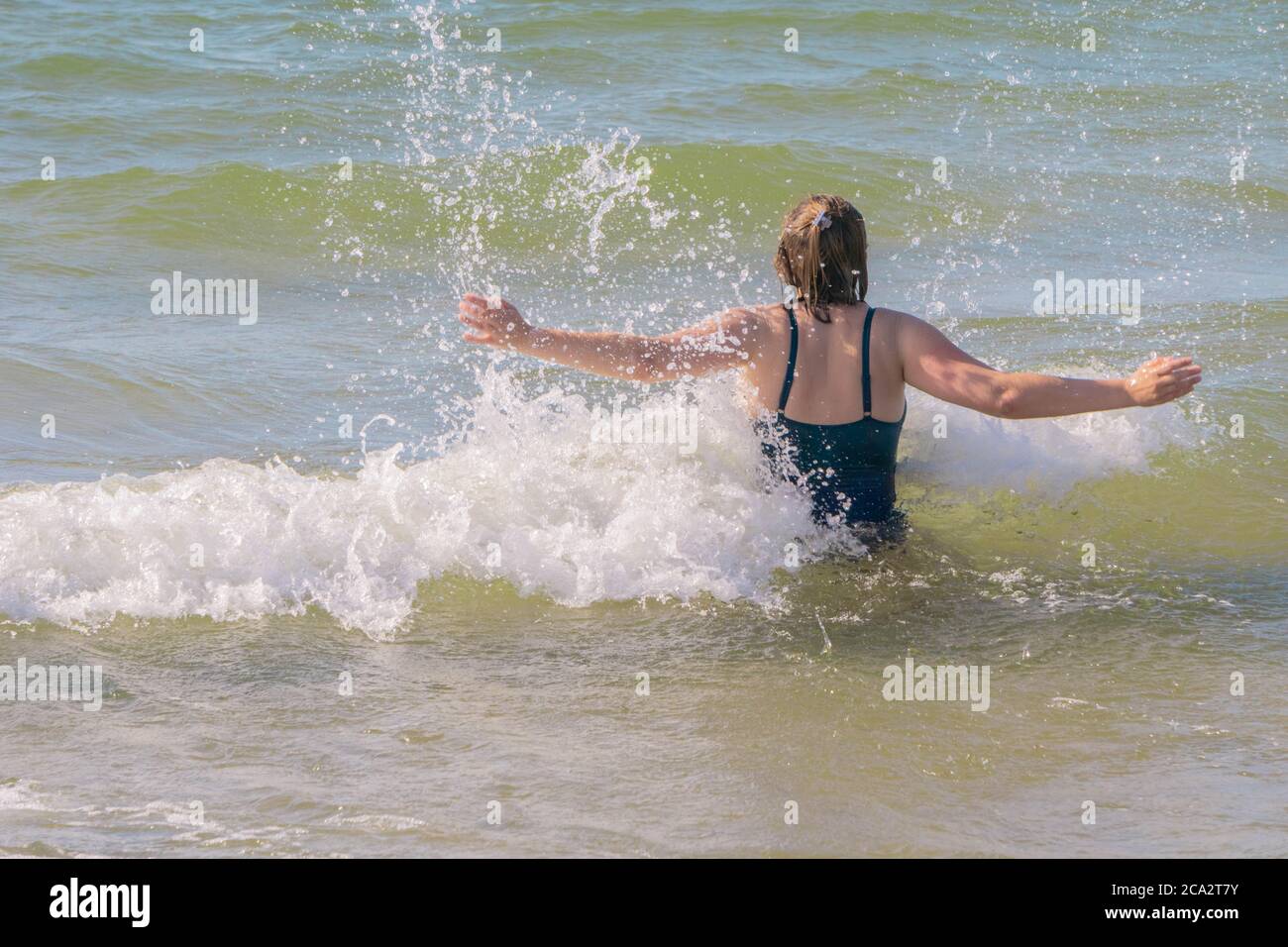 Woman in waving sea doing splashes of water with open hands. Woman ...