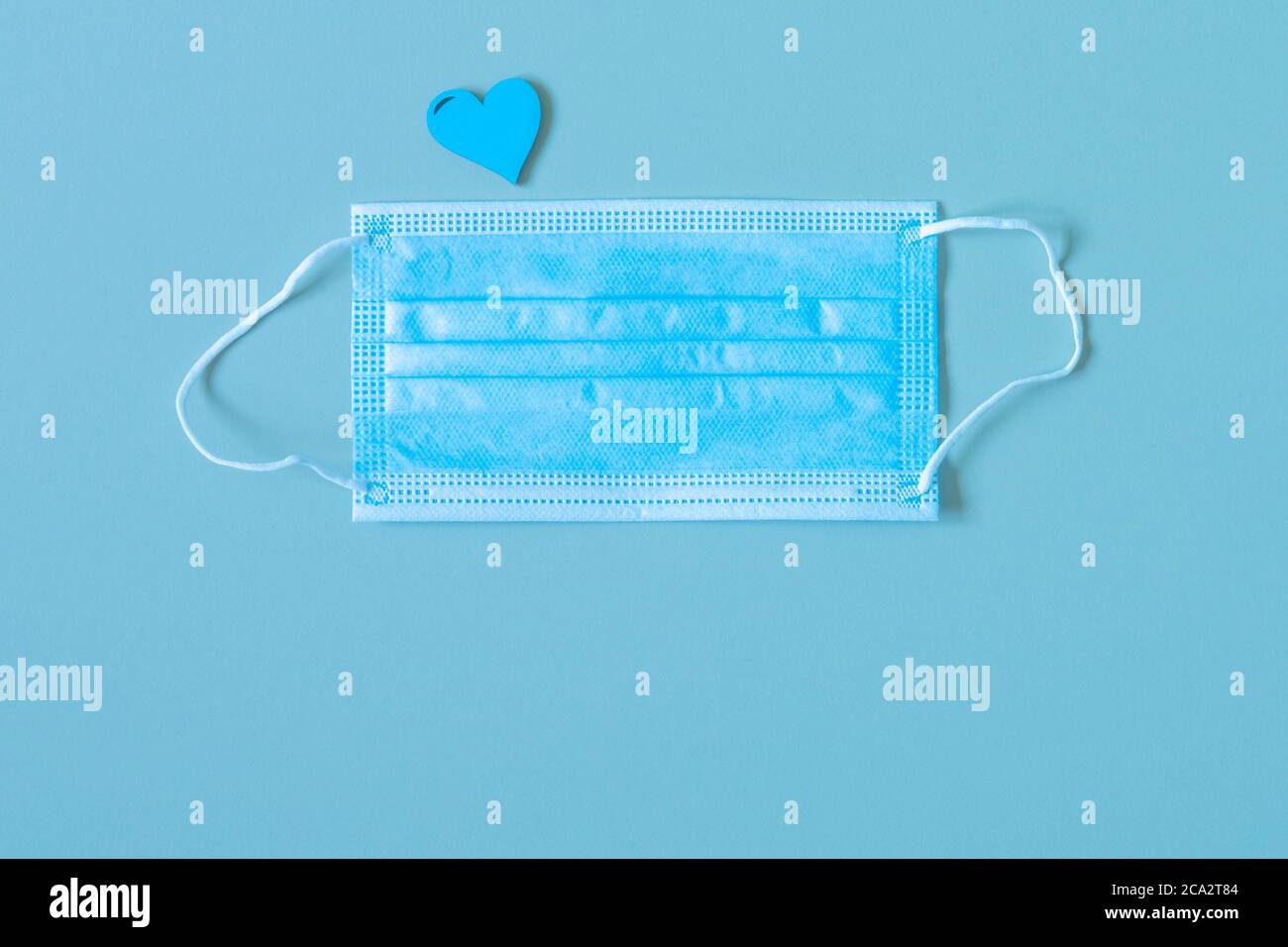 Flat lay of disposable medical mask and symbol of heart. Blue facemask ...