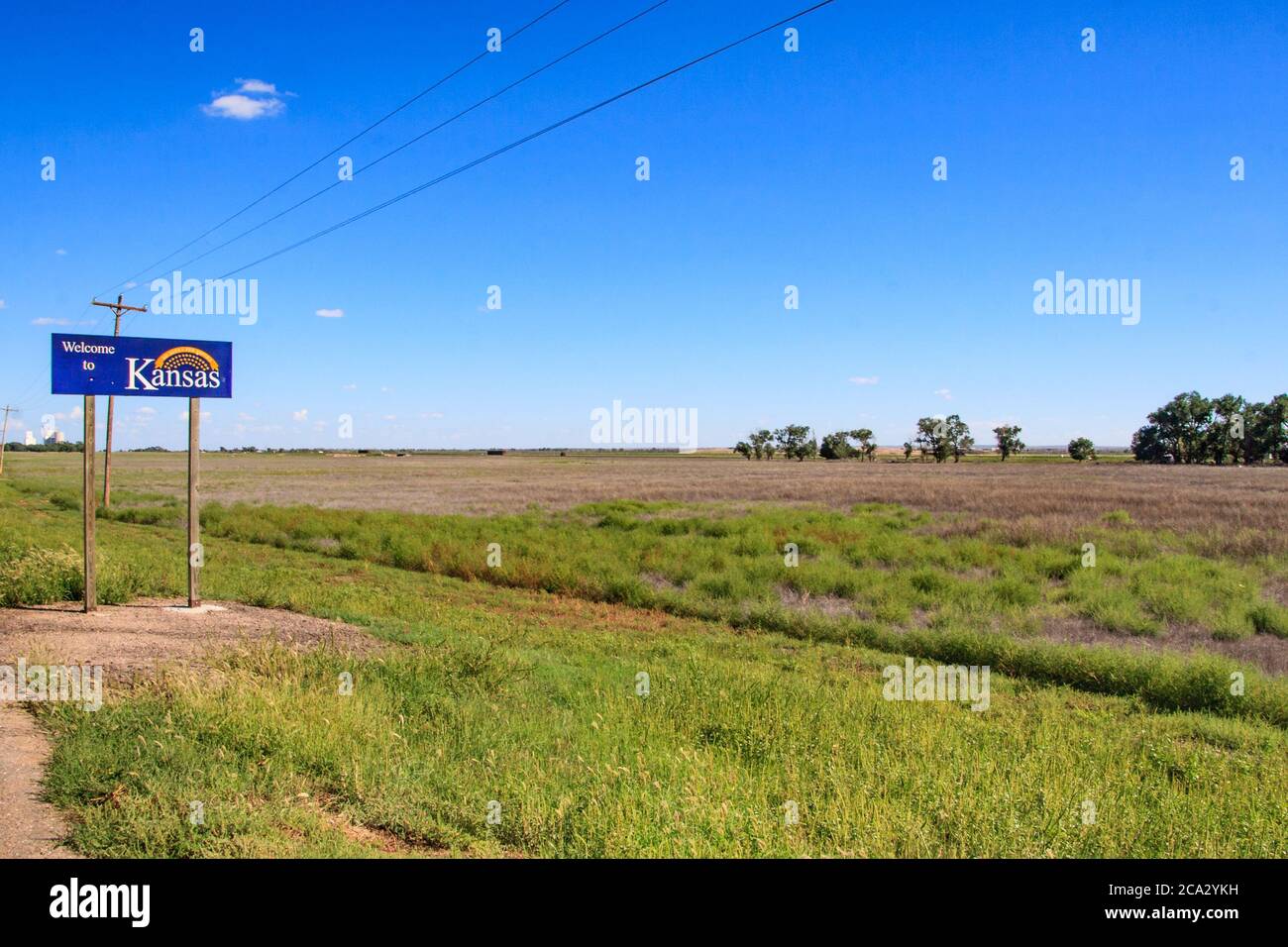 A 'Welcome to Kansas' sign in the countryside, with a blue sky overhead ...
