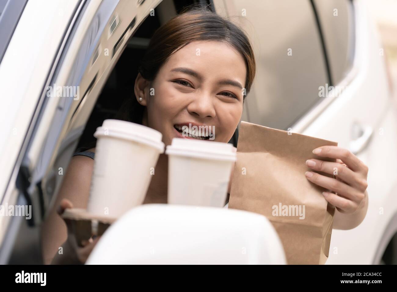 Asian Young adult in car holding disposable bag and coffee tray for ...