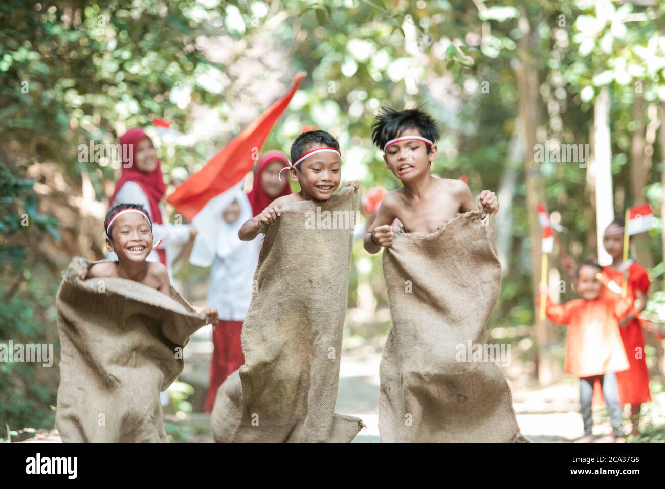 three asian children compete to be the forefront of the sack race with ...