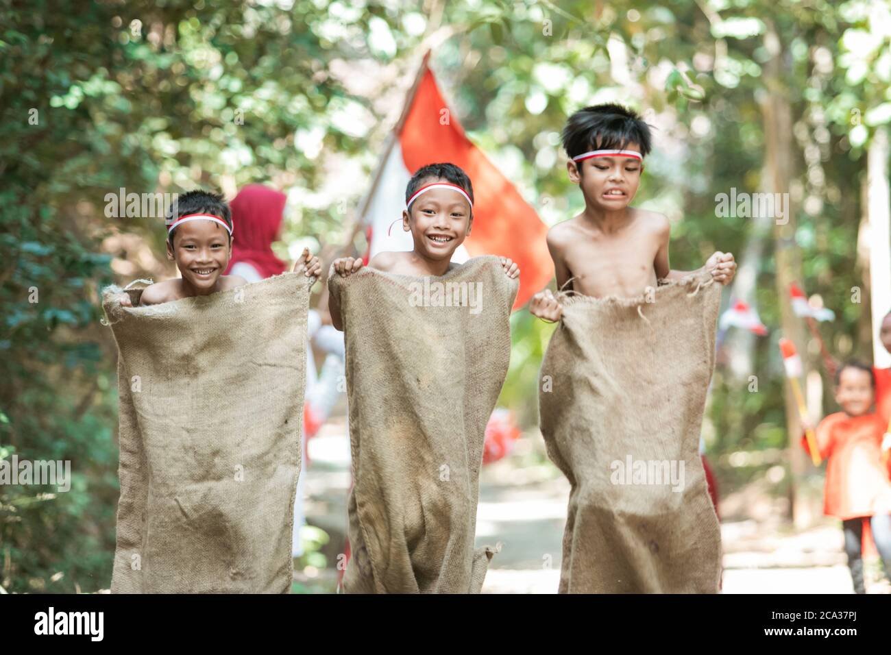 three children try to run fast and jump in the sack race with friends ...