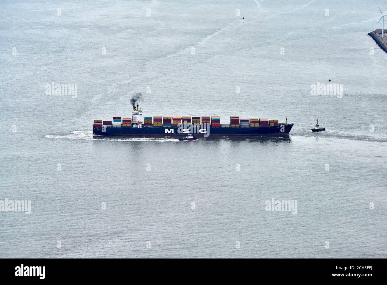 A container ship, being manouvered by two tug boats, in the mouth of ...