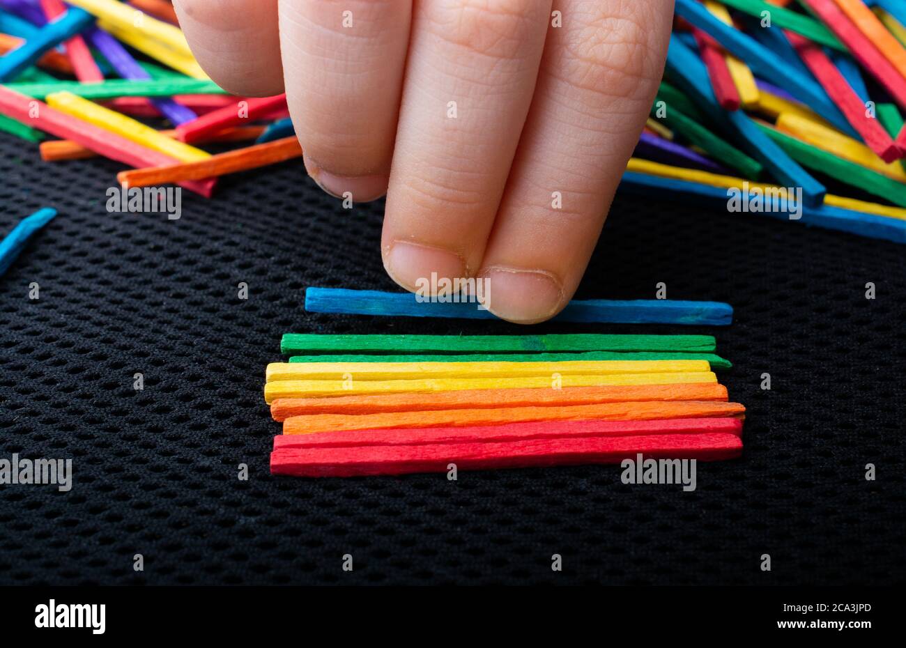 Kid playing with coloured wooden sticks for creativity on white ...