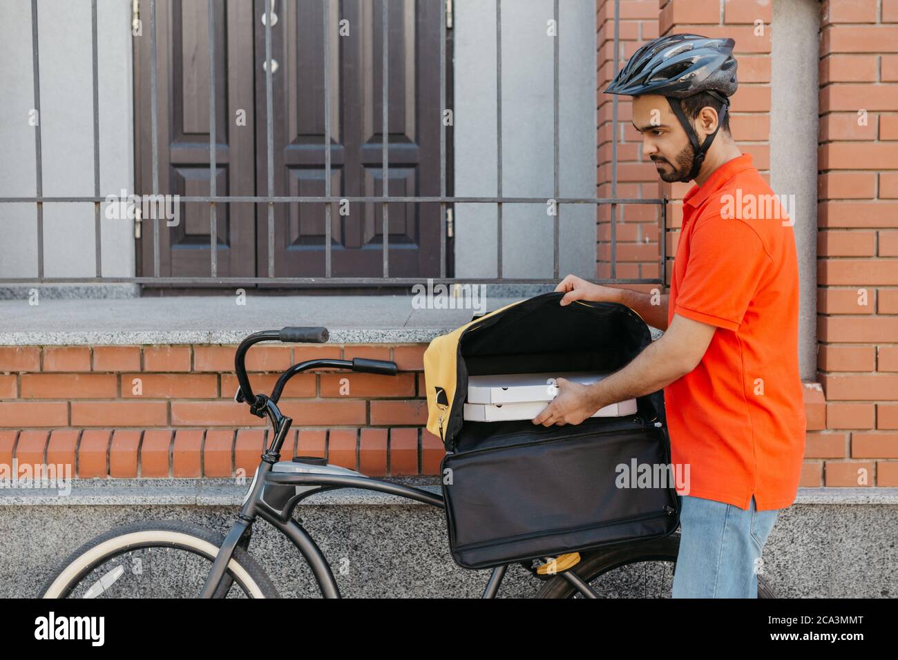 Delivery home and office. Young delivery man takes out pizza from big yellow backpack on bicycle ...