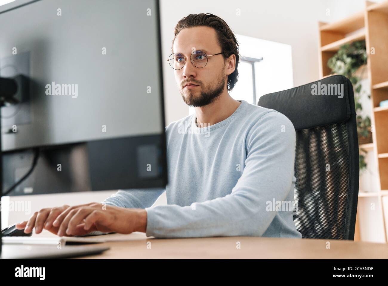 Image of focused unshaven programmer man wearing eyeglasses working with computer in office ...