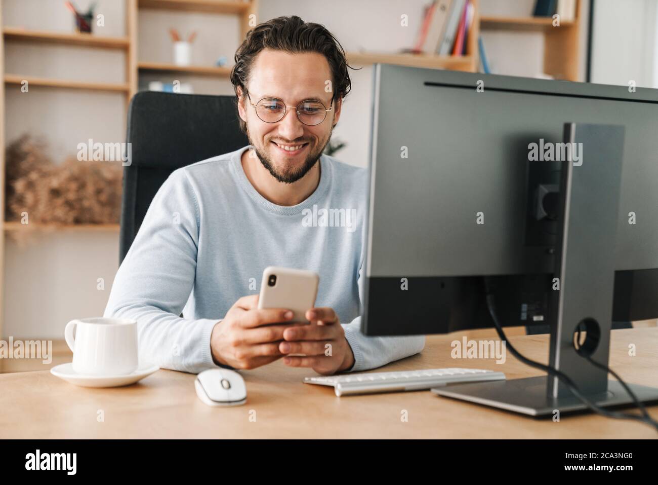 Image of smiling programmer man wearing eyeglasses using cellphone ...