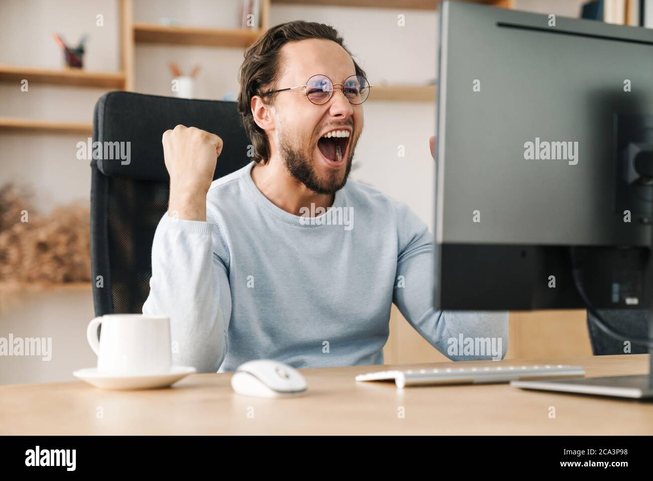 Image of laughing programmer man making winner gesture while working ...