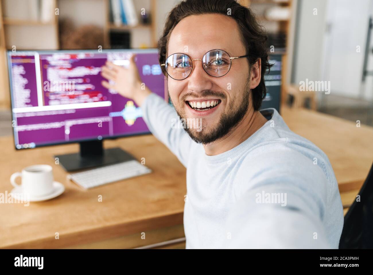 Image of unshaven excited programmer man showing screens while taking ...