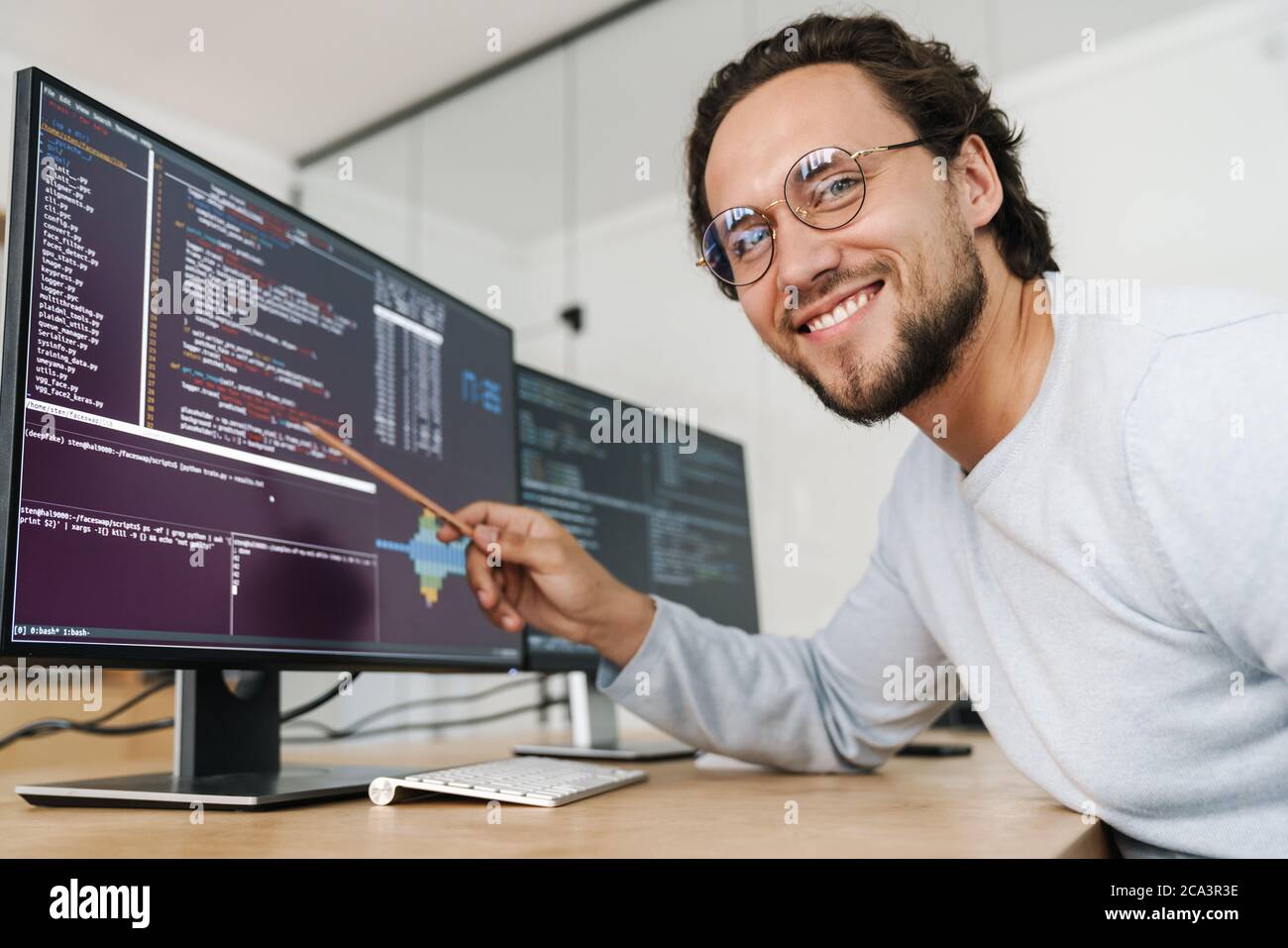 Image of smiling unshaven programmer man wearing eyeglasses working with computers in office ...