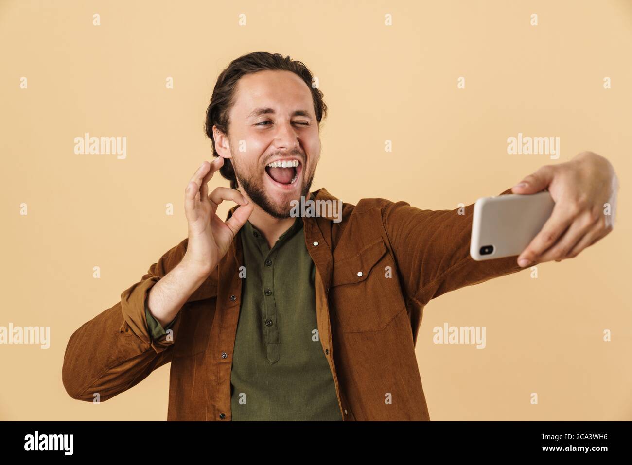 Image of delighted man showing ok sign while taking selfie on cellphone ...