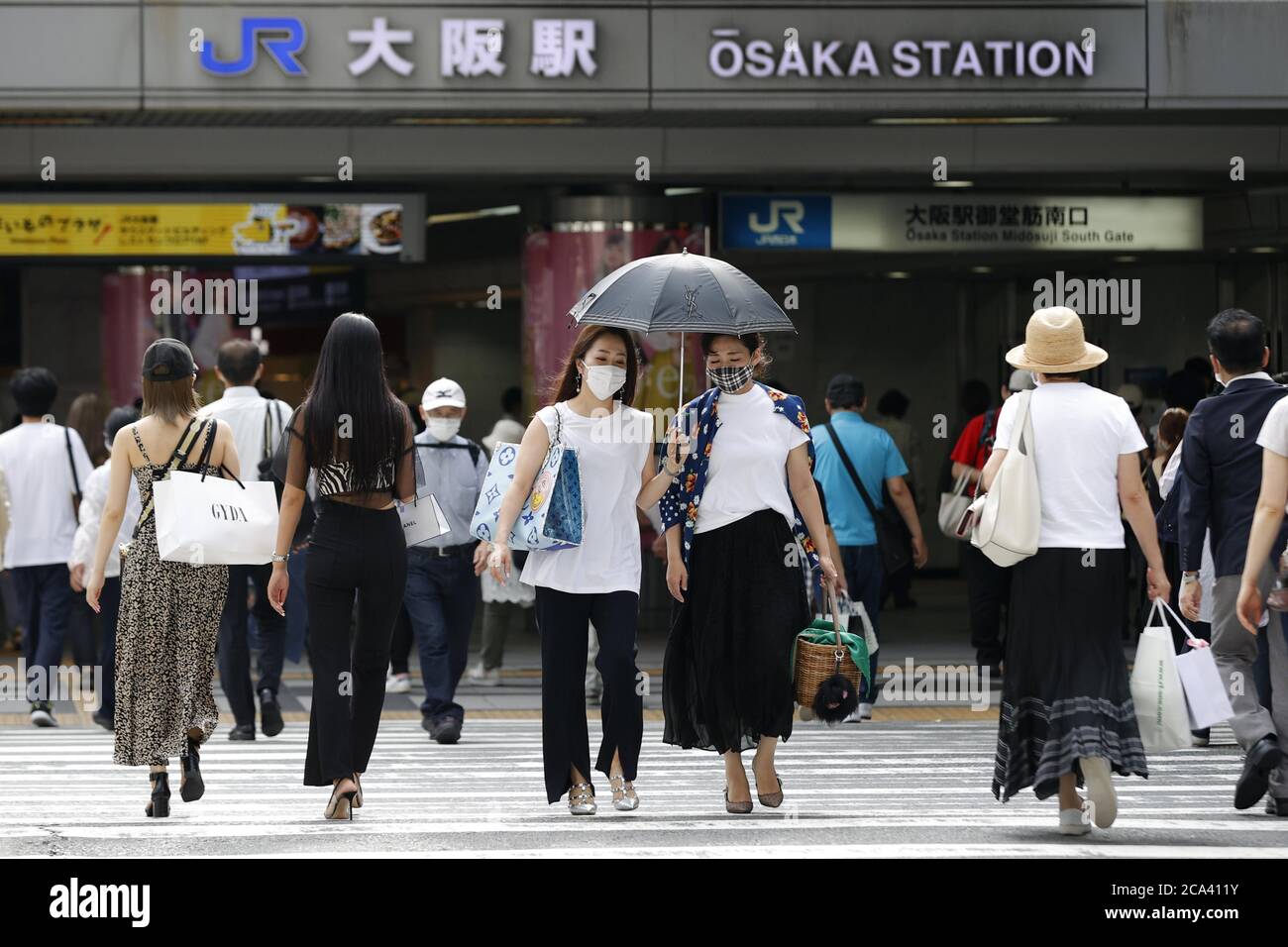 People wearing face masks walk in front of JR Osaka Station in the ...