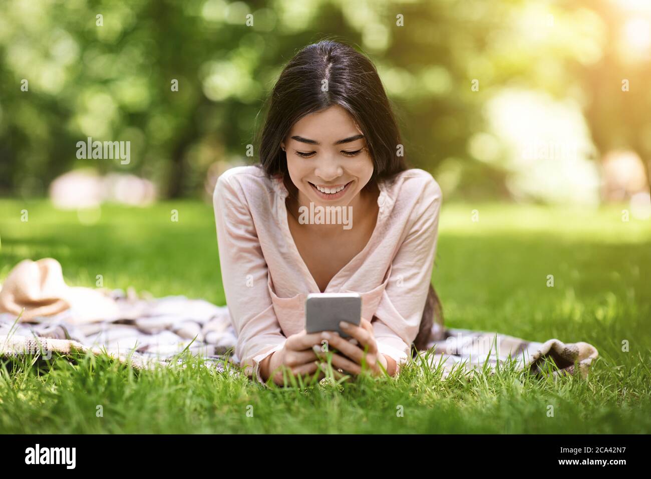 Asian Girl Relaxing With Smartphone On Plaid In Park, Messaging With ...