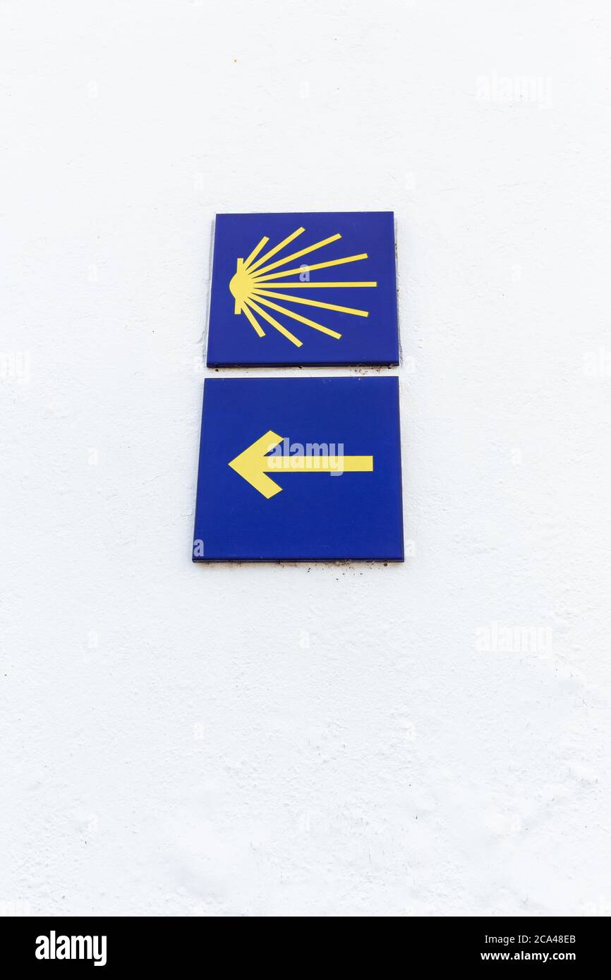 Camino de Santiago Yellow scallop and arrow sign on white wall. Way of ...
