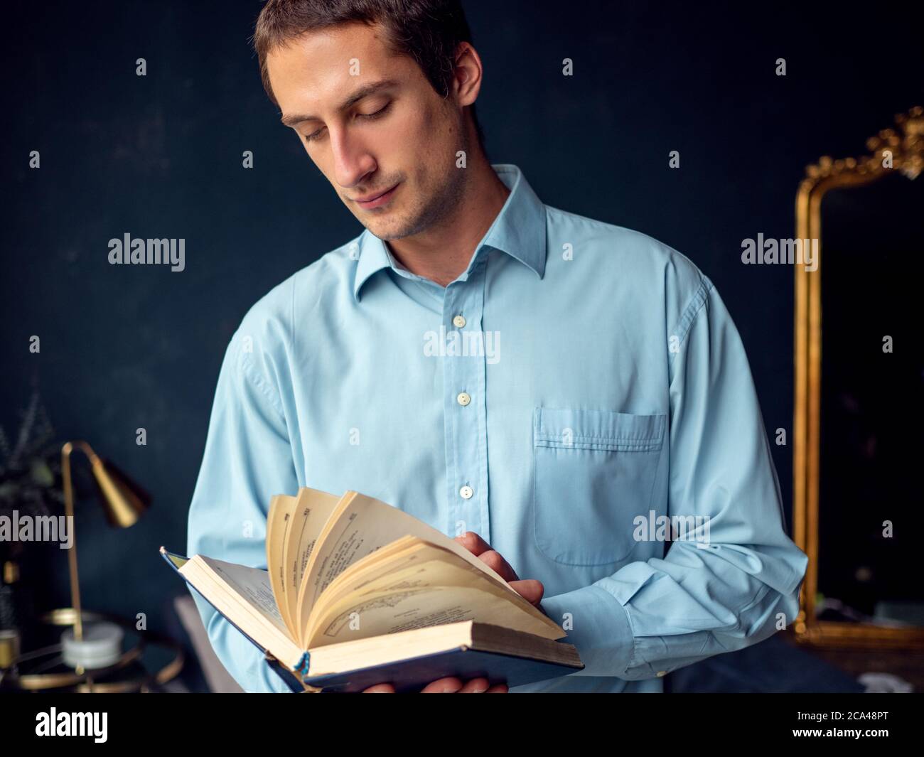 Young man reading a book, a guy in a blue shirt on a dark blue ...