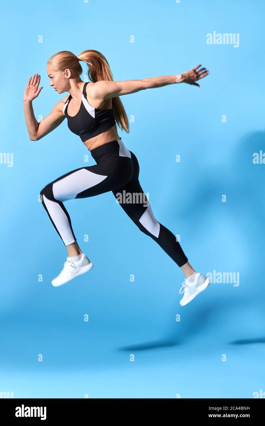 fit strong fair-haired girl is running very fast, isolated blue ...