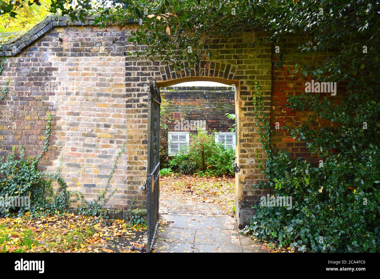 open metal gate with an old brick wall around it Stock Photo - Alamy