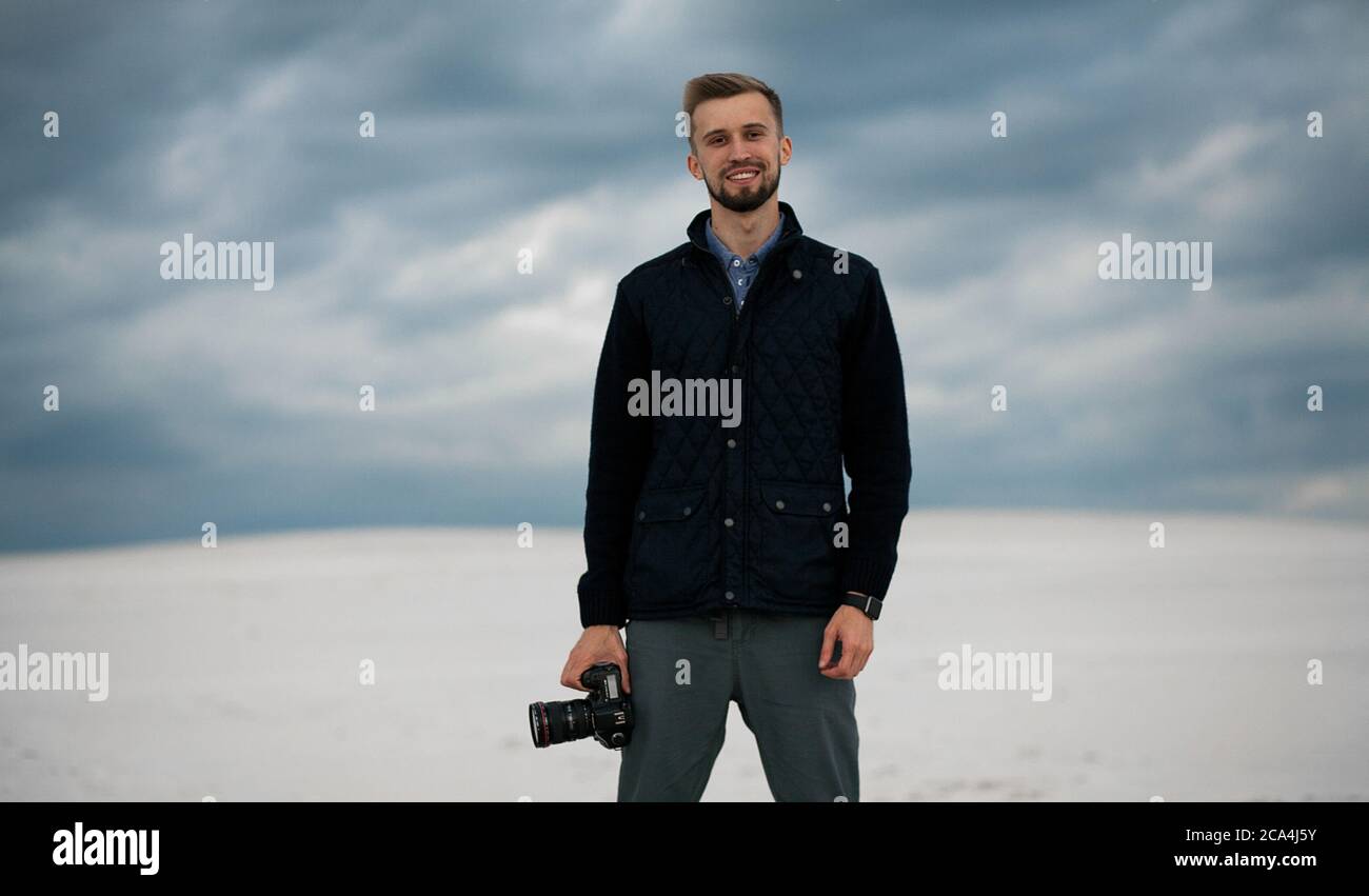 Photographer smiles and stands in desert with digital camera in his ...