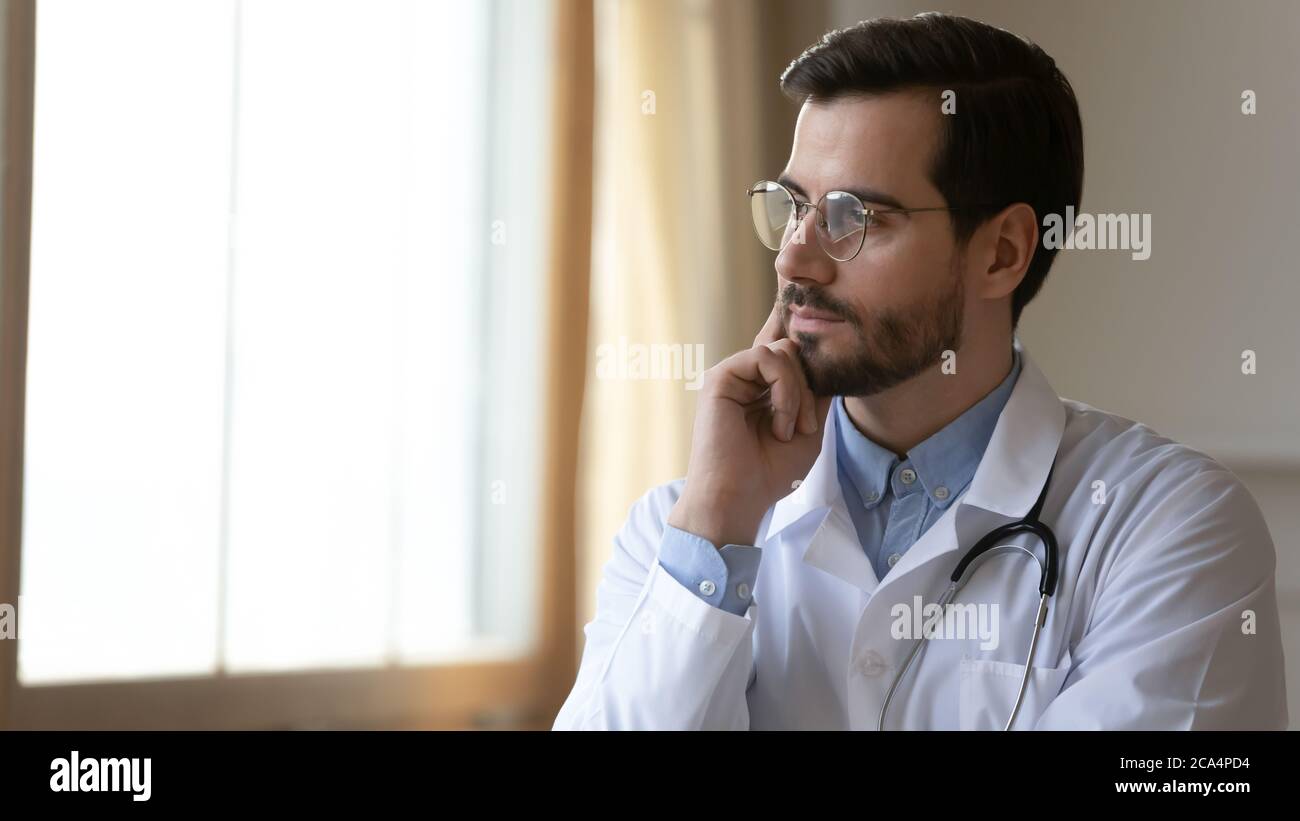 Thoughtful serious young male doctor general thinking of challenges ...