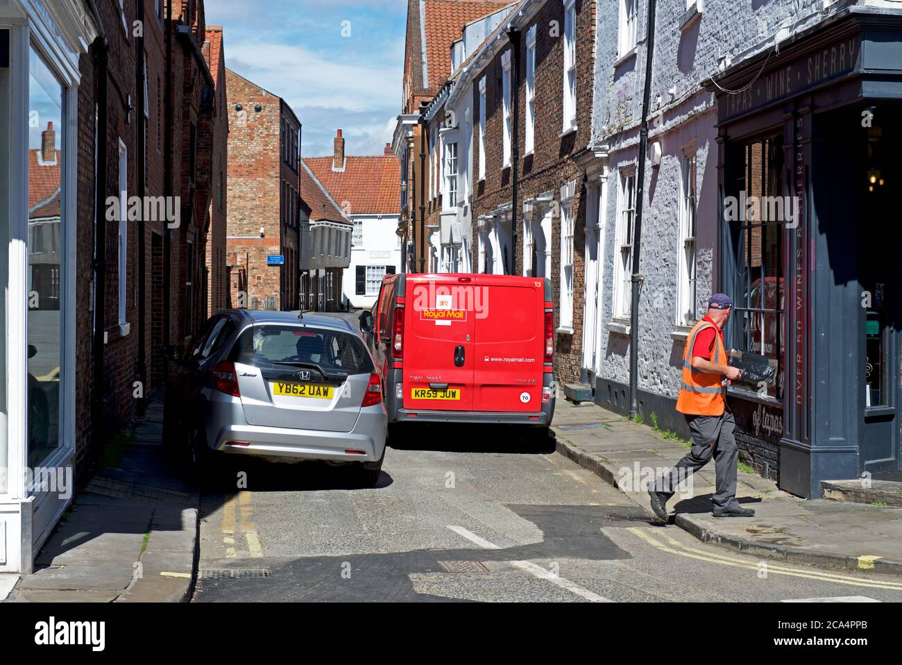Postman delivering a package, as his Royal Mail van blocks narrow ...