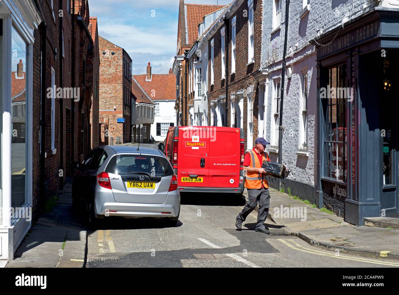 Postman delivering a package, as his Royal Mail van blocks narrow ...