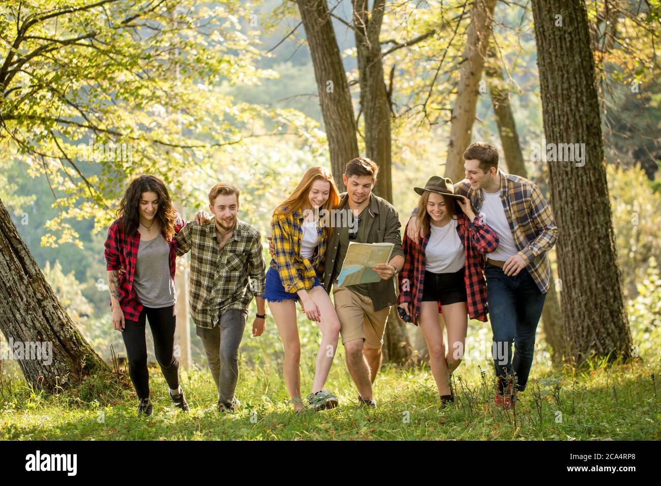 positive young tourists walking with a map in the forest, full length ...
