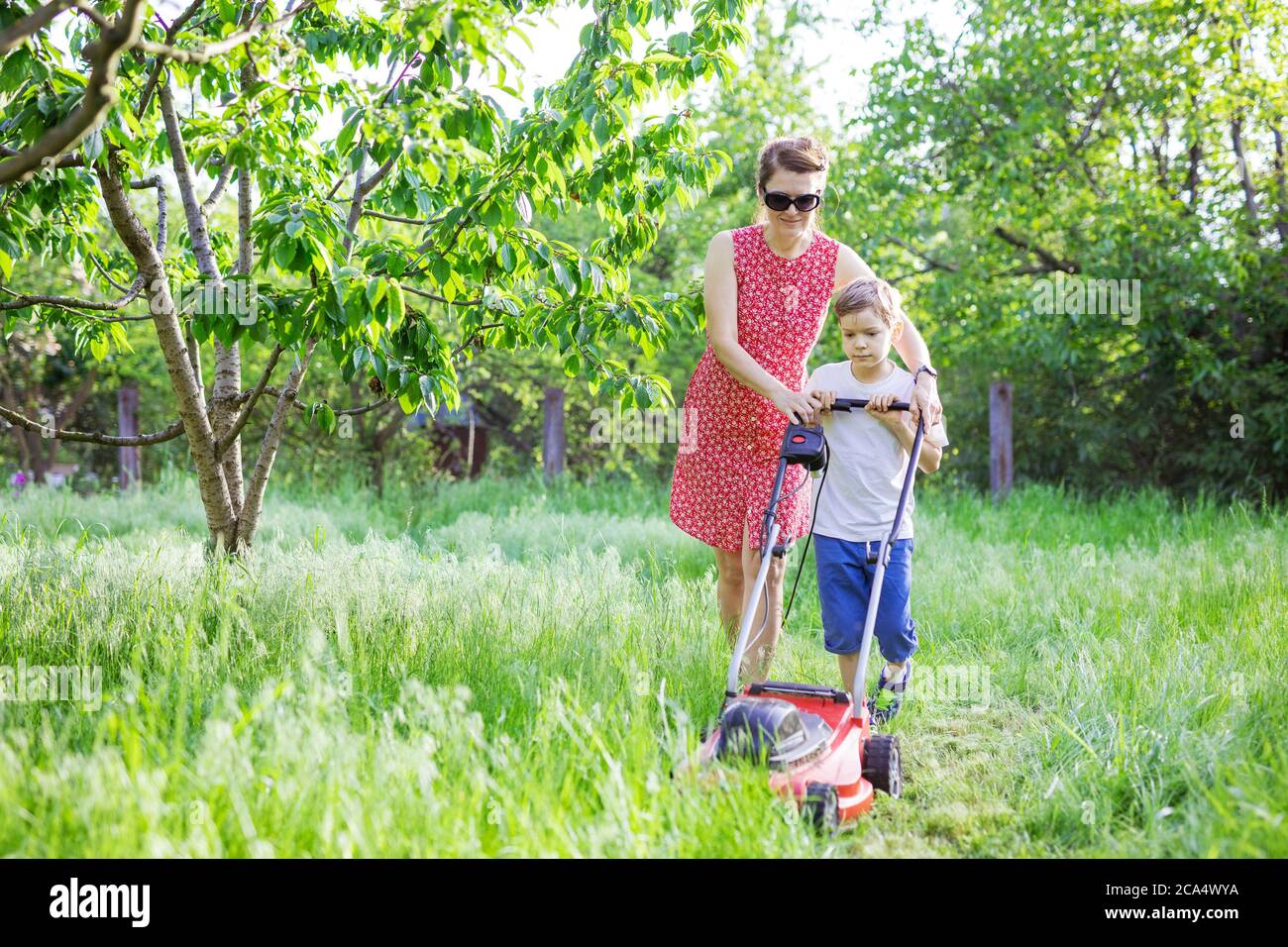 Mother and son mowing grass with lawnmower in garden Stock Photo - Alamy