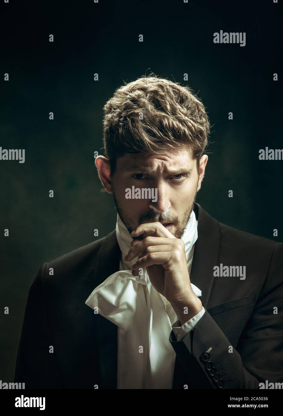 Sincere sin. Young man in suit as Dorian Gray isolated on dark green ...