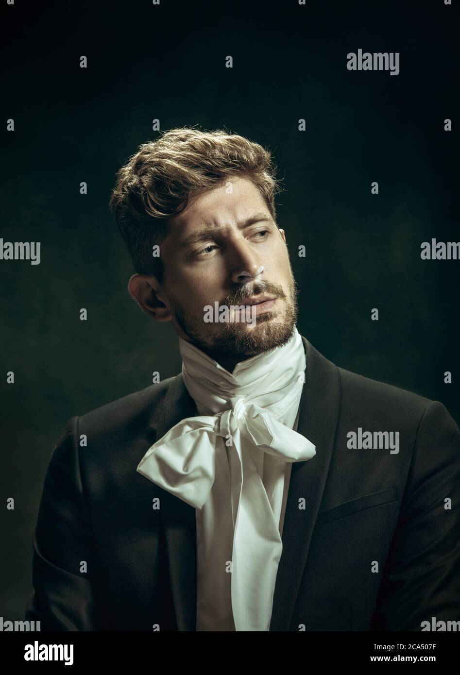 Sincere sin. Young man in suit as Dorian Gray isolated on dark green ...