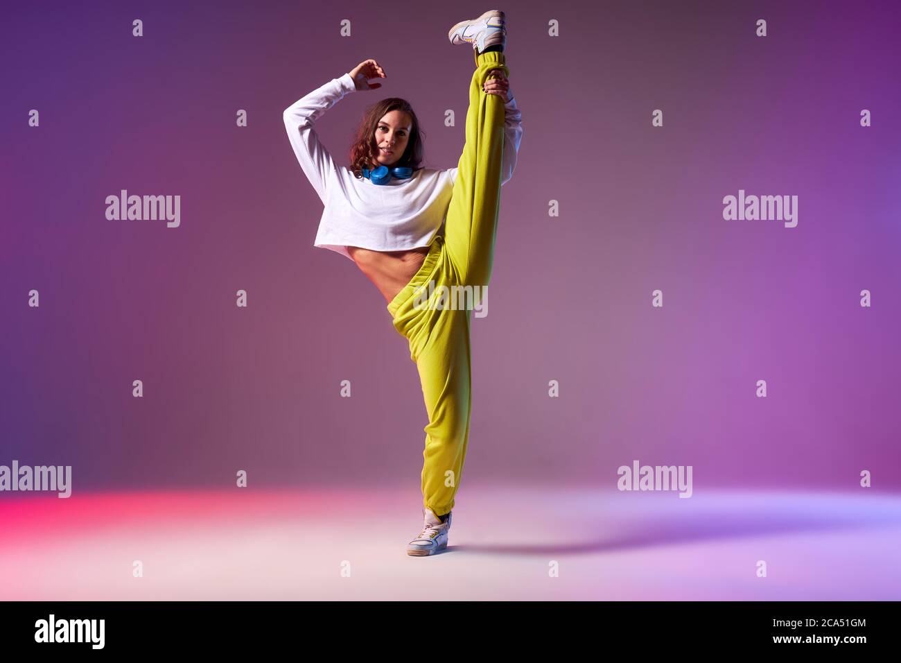 Flexible young dancer dressed in brightly coloured clothes, raising leg ...