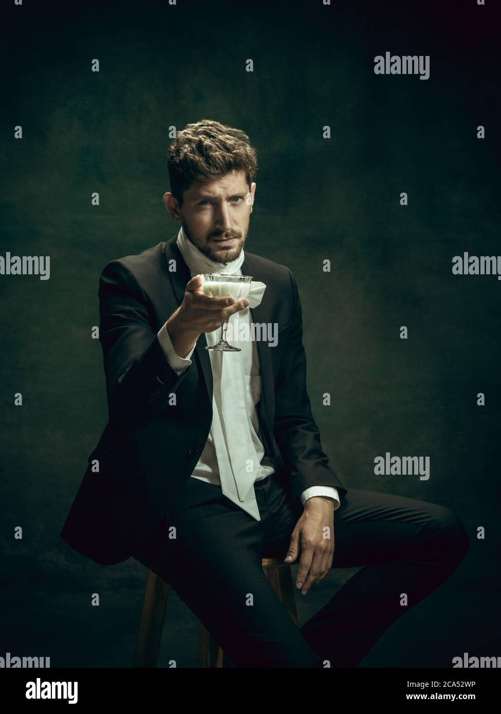 Drinking liquor. Young man in suit as Dorian Gray isolated on dark ...