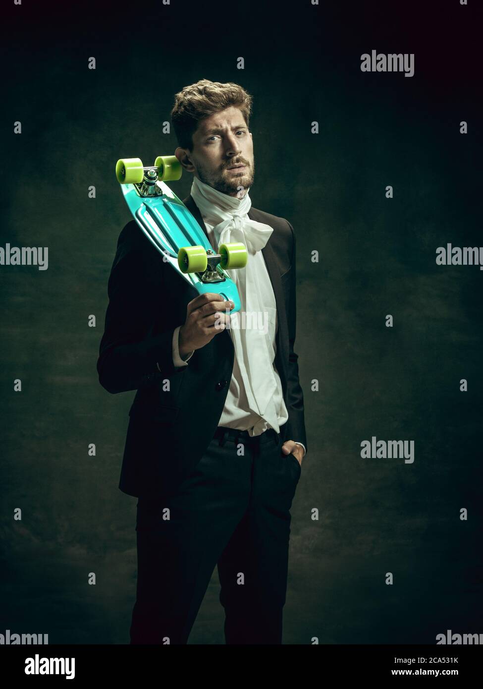 Skateboard. Young man in suit as Dorian Gray isolated on dark green ...