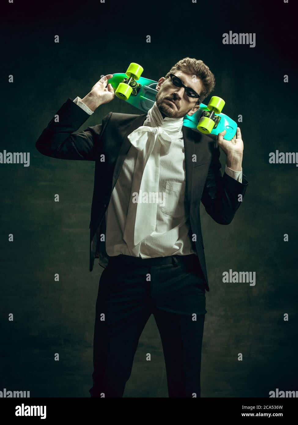 Skateboard. Young man in suit as Dorian Gray isolated on dark green ...