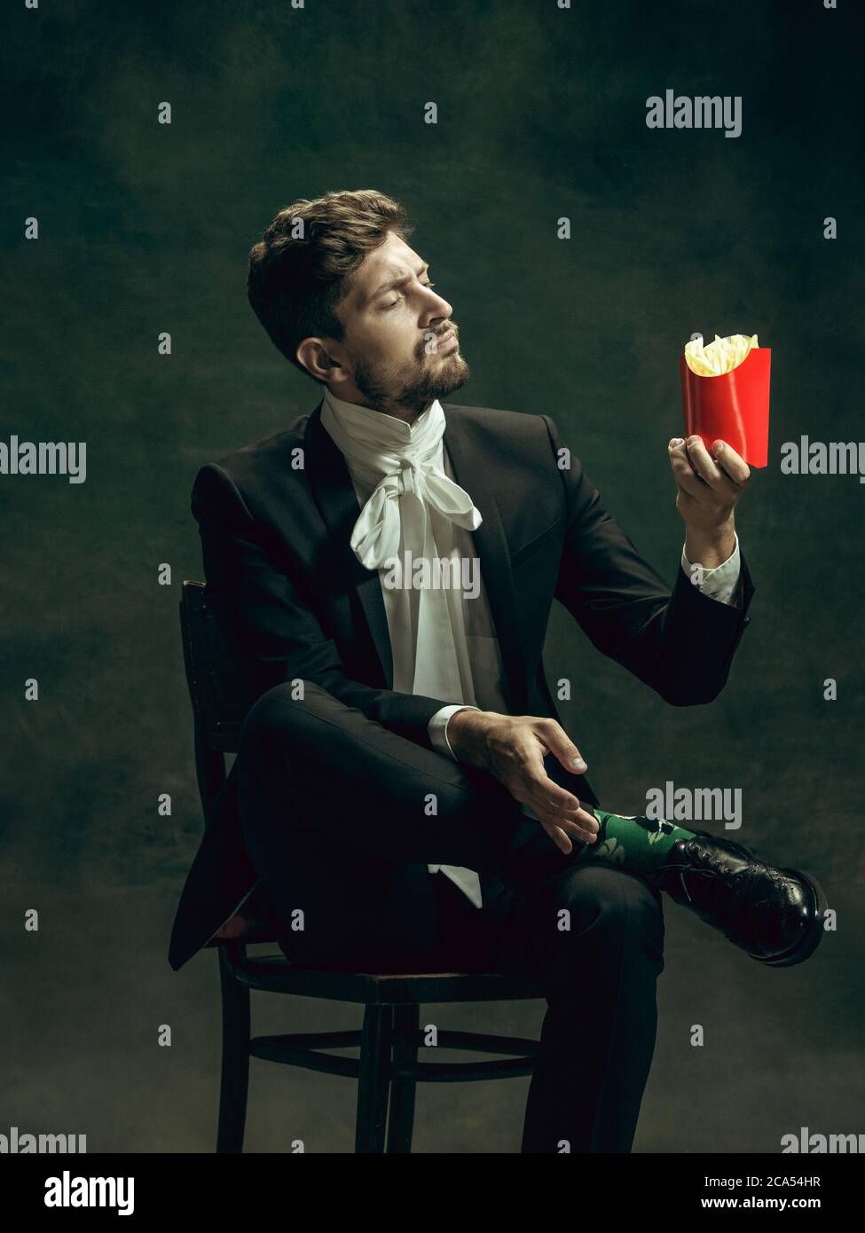 Enjoy urban food. Young man in suit as Dorian Gray isolated on dark ...