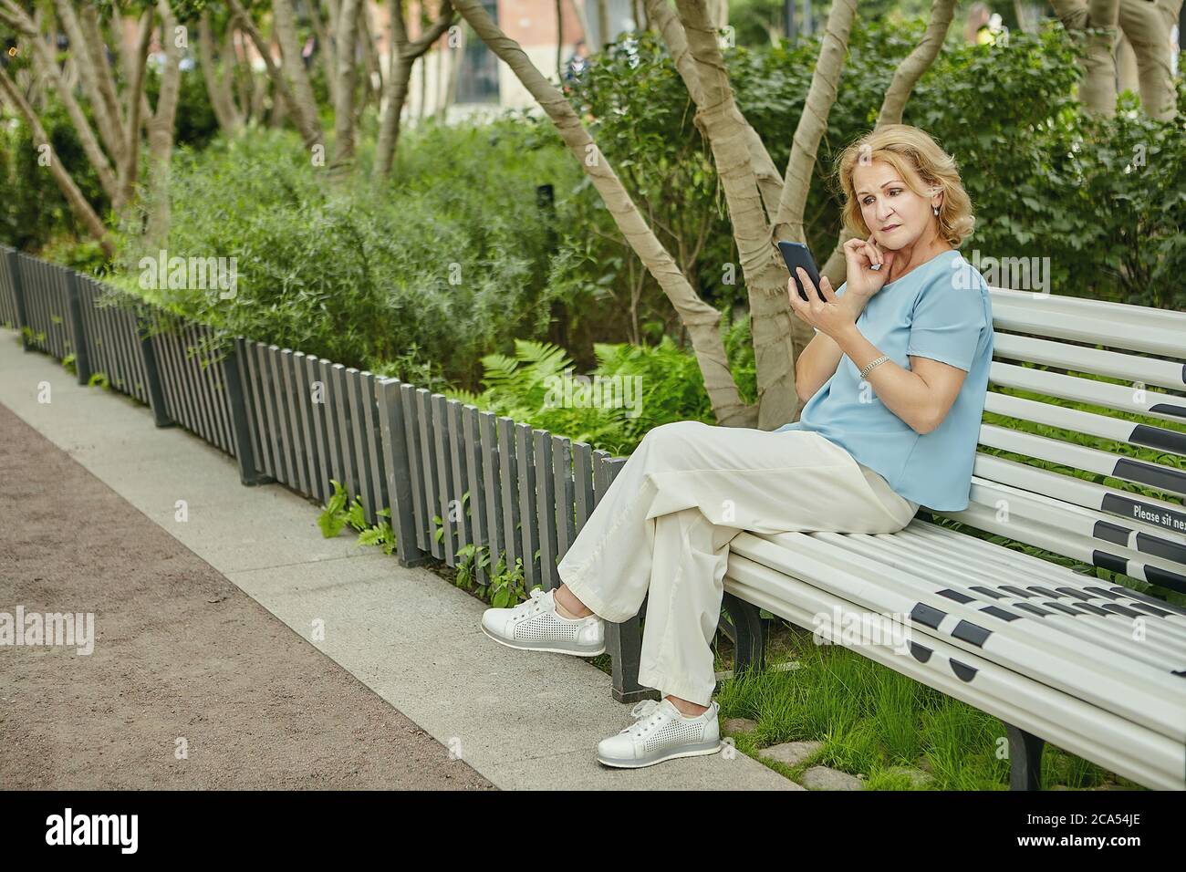 Elderly pretty white woman about 62 years old is sitting on the bench ...