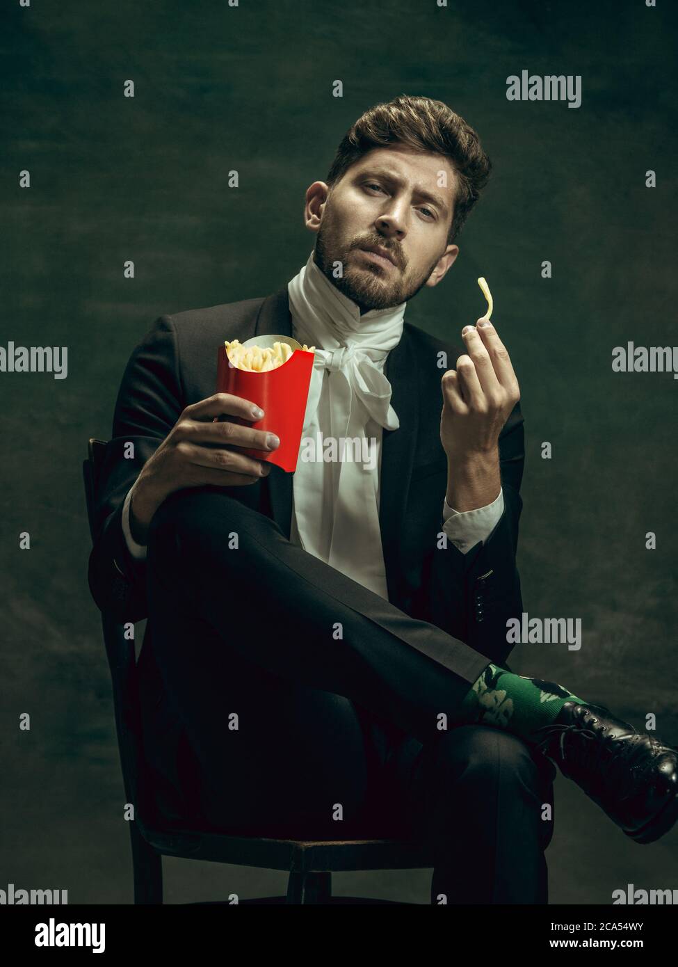 Enjoy urban food. Young man in suit as Dorian Gray isolated on dark ...