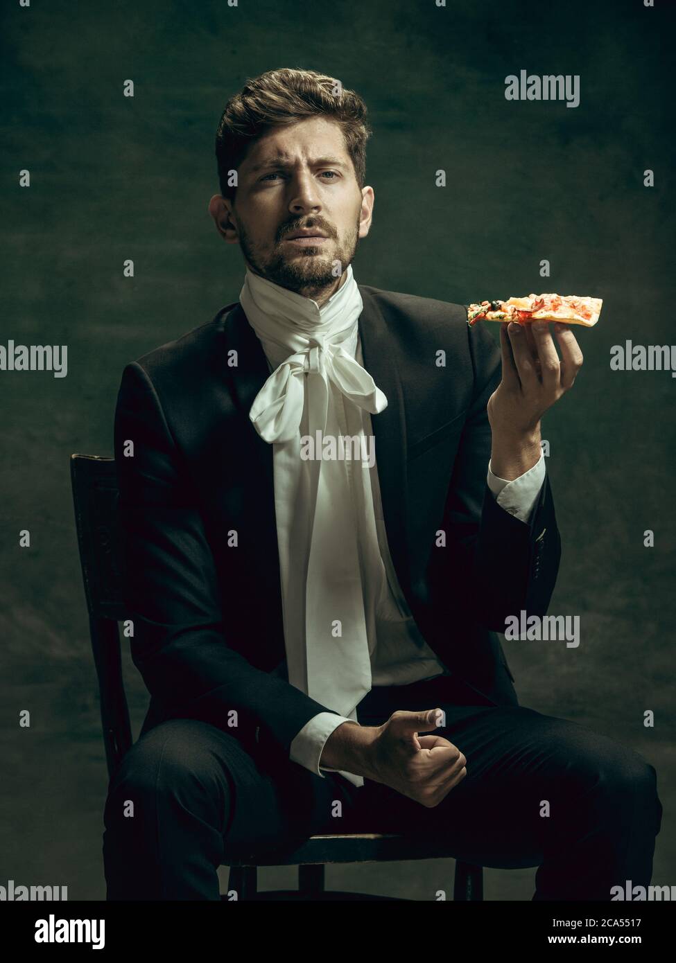 Tasting pizza. Young man in suit as Dorian Gray isolated on dark green ...