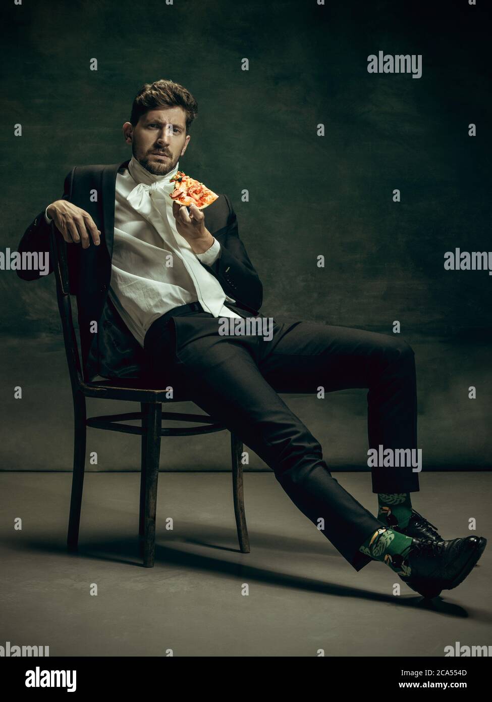 Tasting pizza. Young man in suit as Dorian Gray isolated on dark green ...