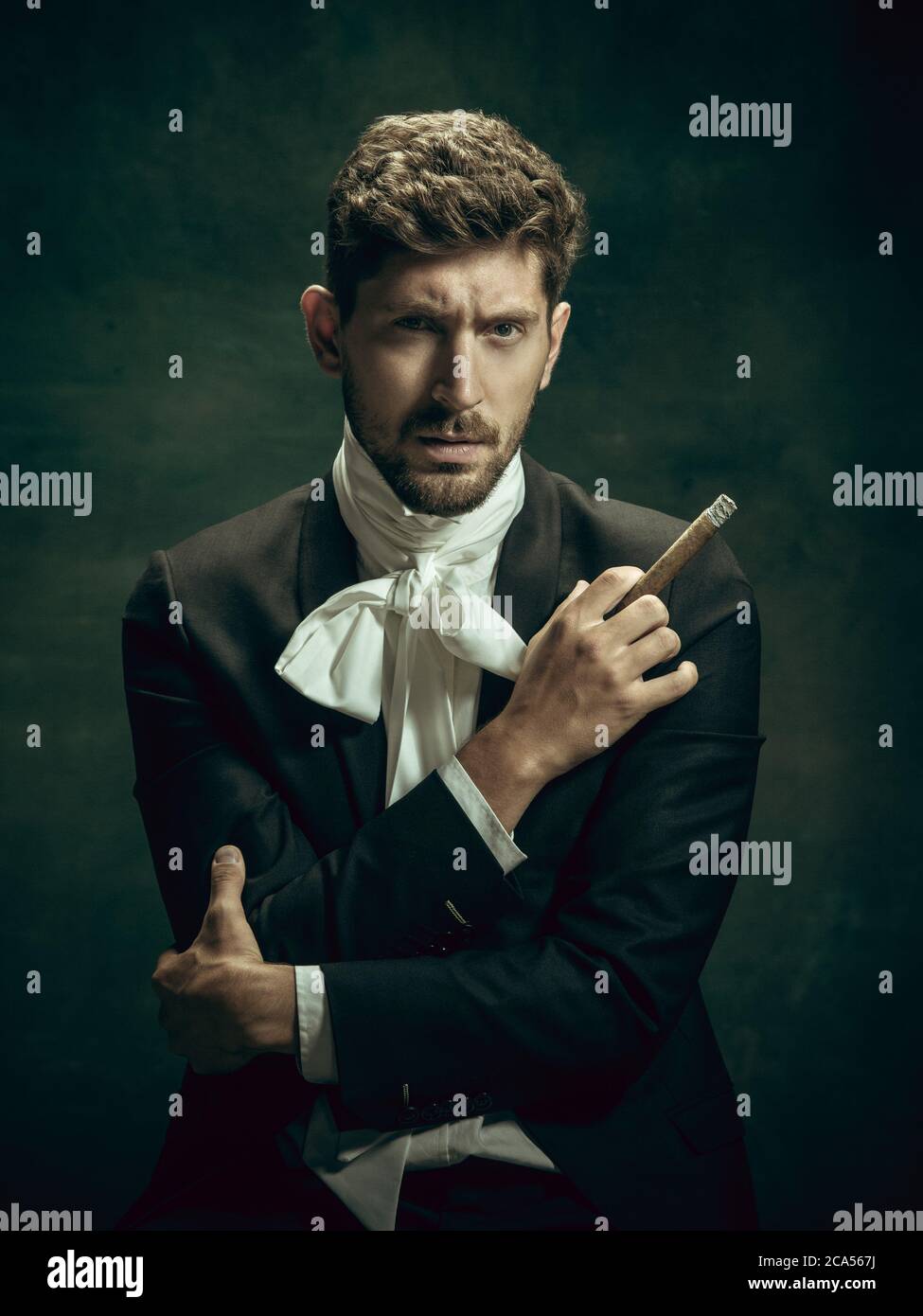 Brutal smokes cigar. Young man in suit as Dorian Gray isolated on dark ...