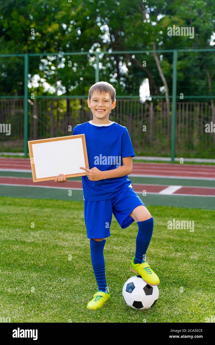 a small soccer player with a ball stands on a green soccer field with a ...