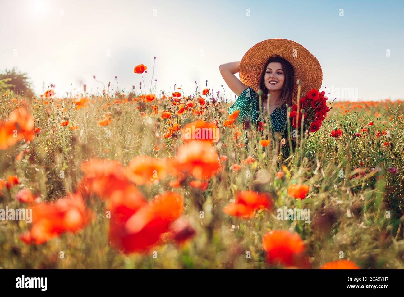 Young woman picking poppies flowers walking in summer field enjoying ...