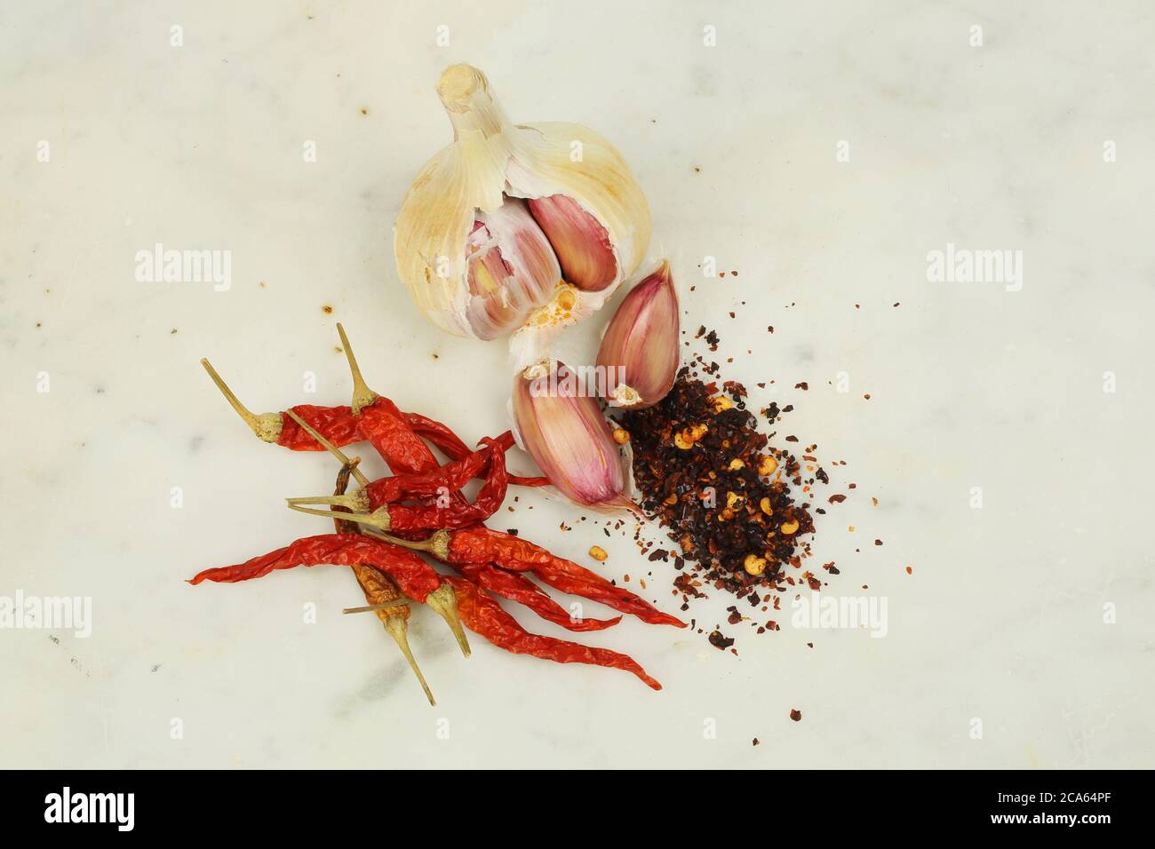 Garlic bulb and clove with dried and flaked chilli on a marble work ...