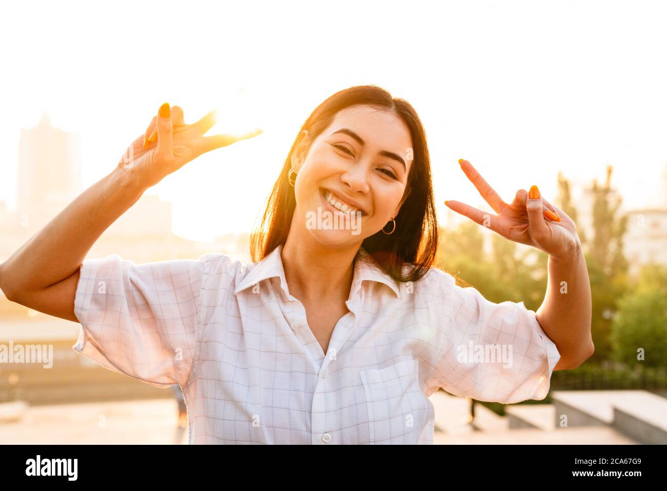 Photo of joyful beautiful asian woman laughing and gesturing peace sign ...