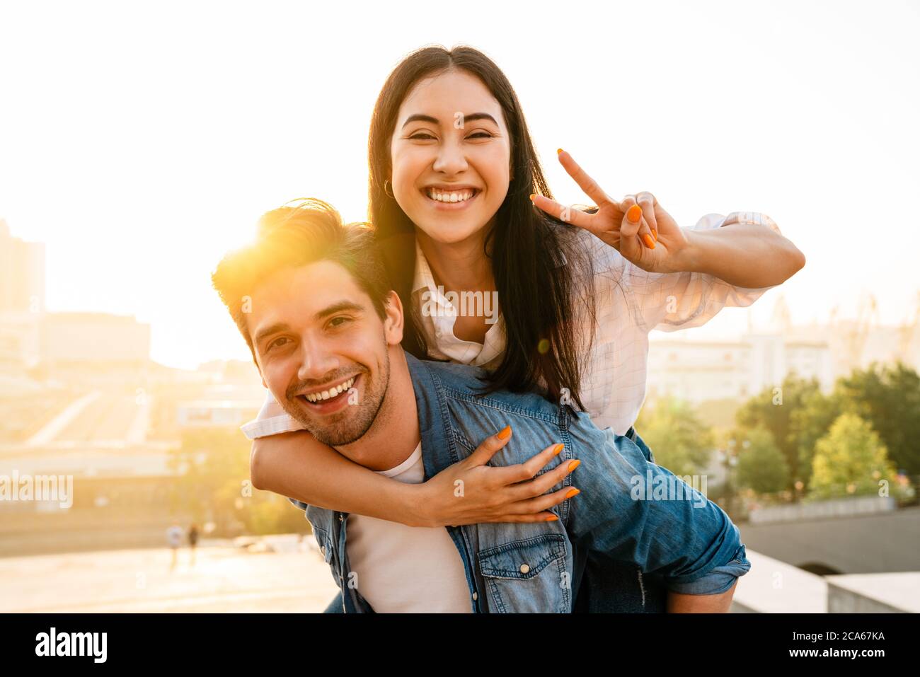 Image of cheerful multicultural couple piggybacking ride and gesturing ...