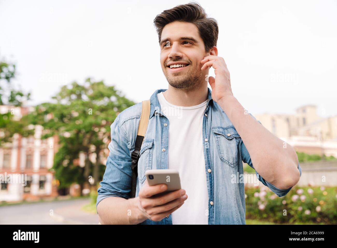 Photo of smiling man with wireless earphone using cellphone while ...